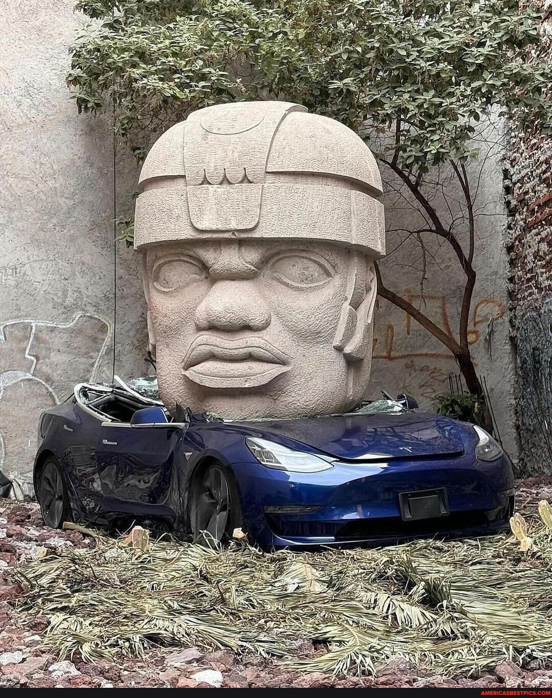 A tesla model 3 being crushed by an olmec head. it symbolizes the ...